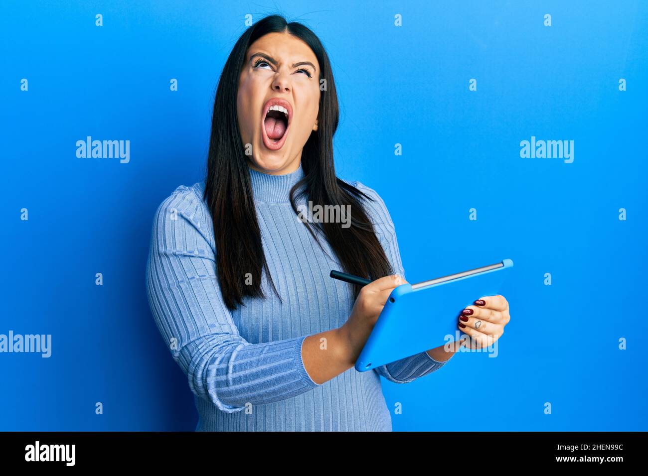 Beautiful brunette woman using touchpad drawing on screen angry and mad ...