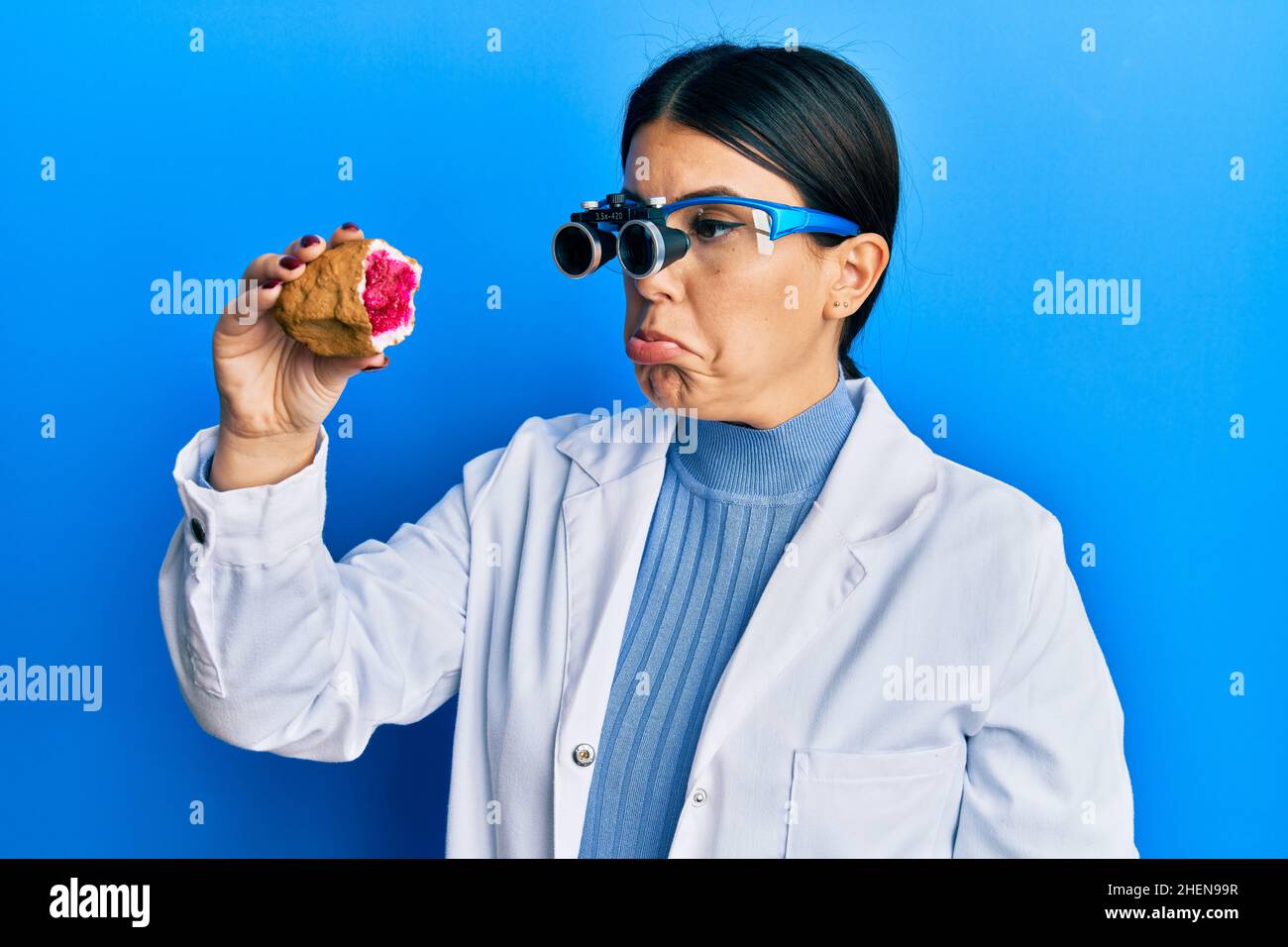 Beautiful brunette jeweller woman holding geode stone wearing magnifier ...