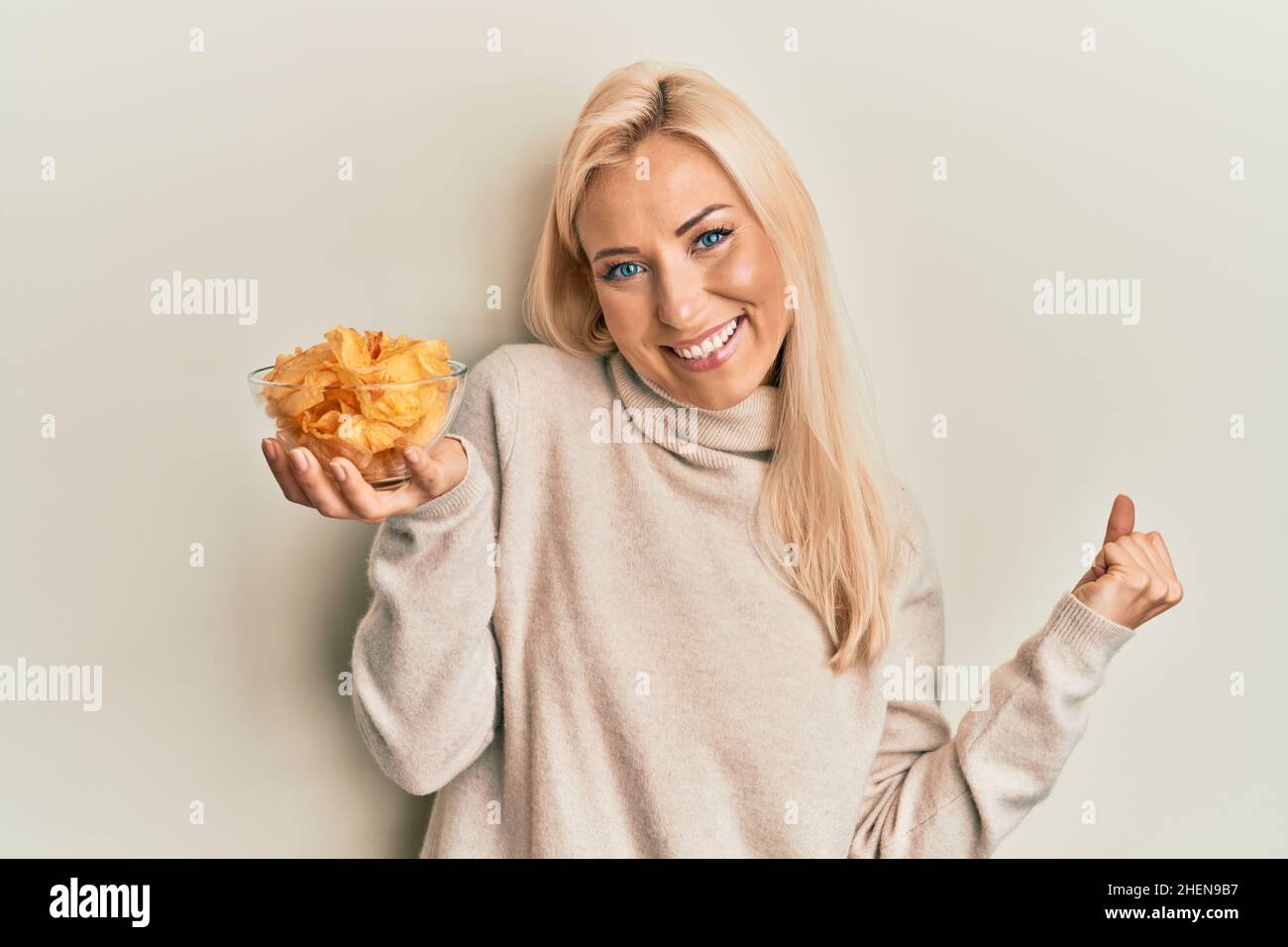 Young blonde woman holding bowl with potato chip screaming proud ...