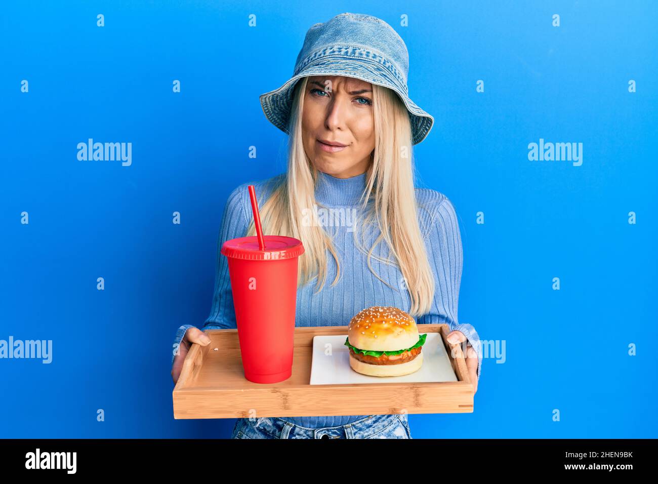 Young blonde woman eating a tasty classic burger and soda clueless and ...