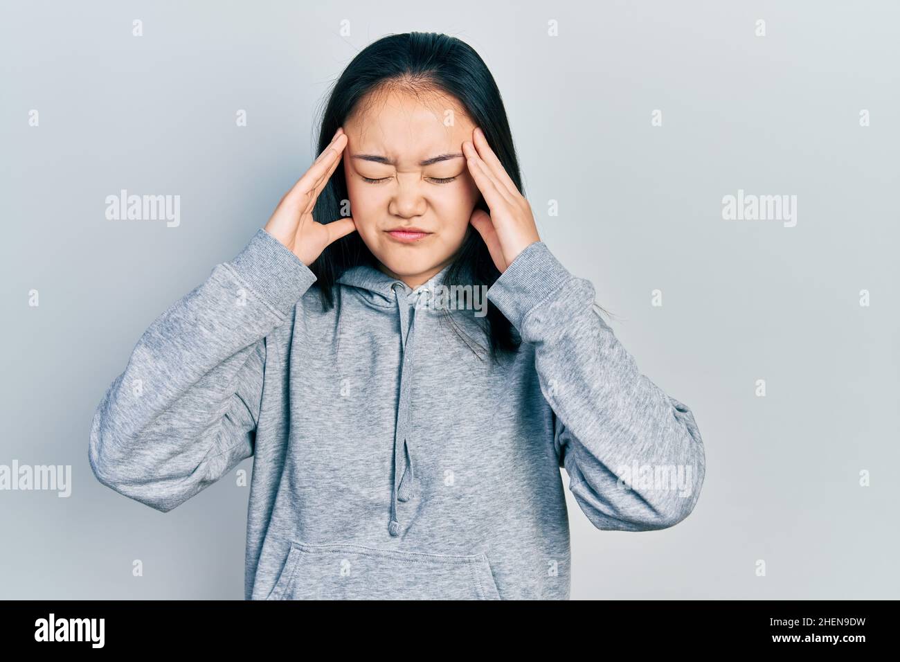 Young chinese girl wearing casual clothes suffering from headache ...