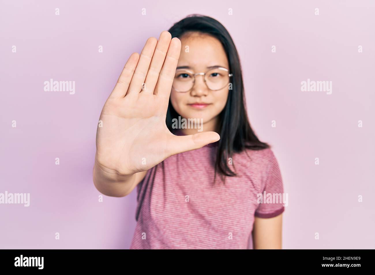 Young chinese girl wearing casual clothes and glasses doing stop sing ...