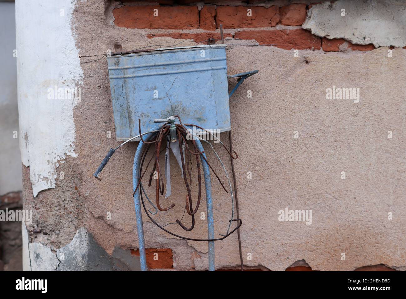 A very old metal water bucket with a faucet hanging on the wall of the ...