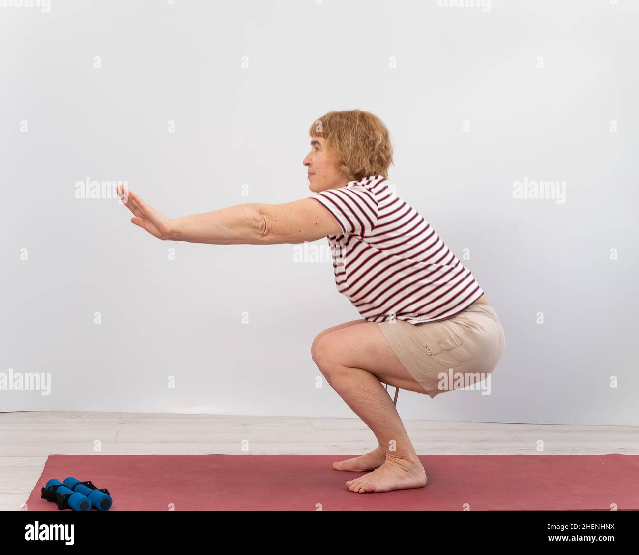 Elderly woman doing squats on a white background. The old lady is doing ...