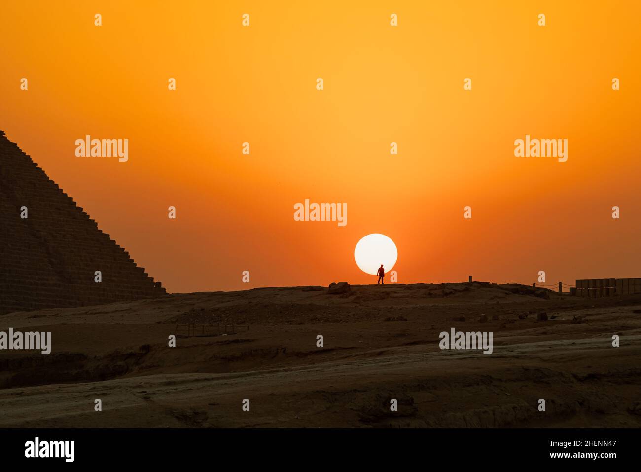 The sun is going down behind the pyramid and a silhouette of a man ...