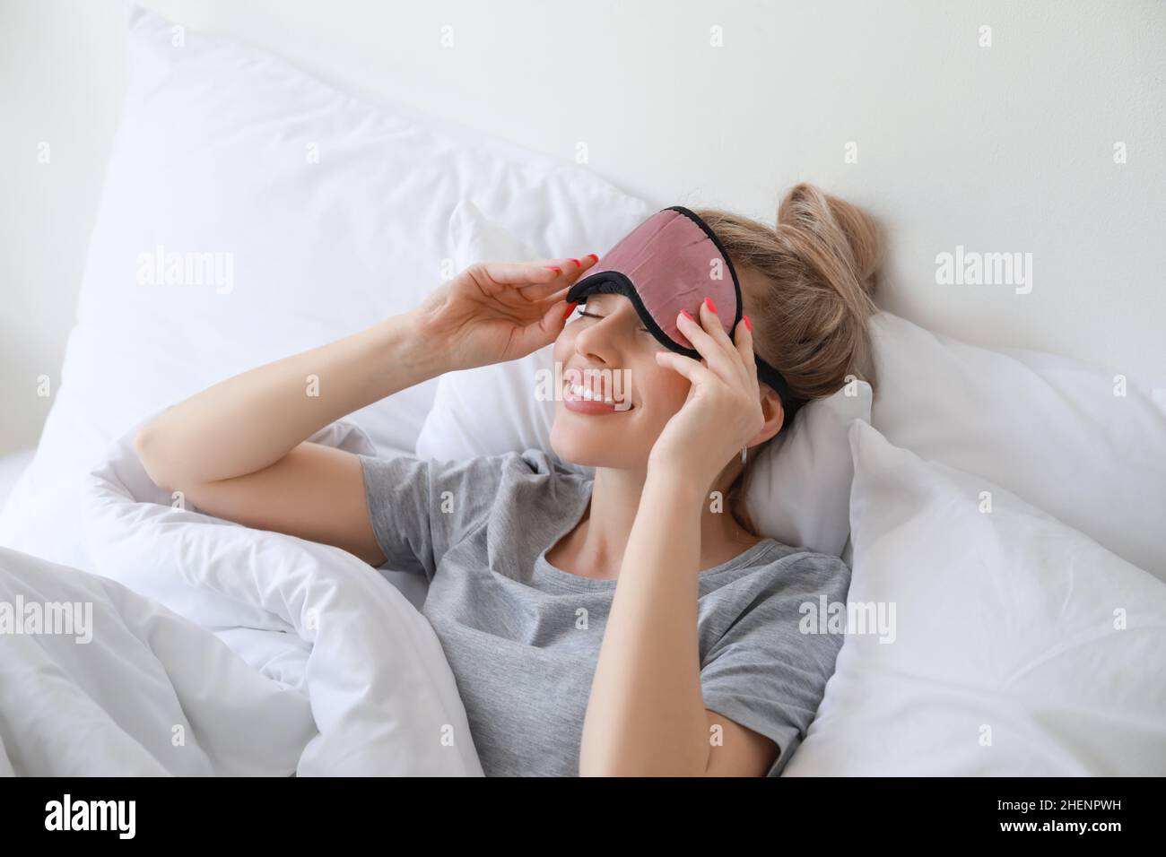 Beautiful young woman taking off sleeping mask in bed Stock Photo - Alamy
