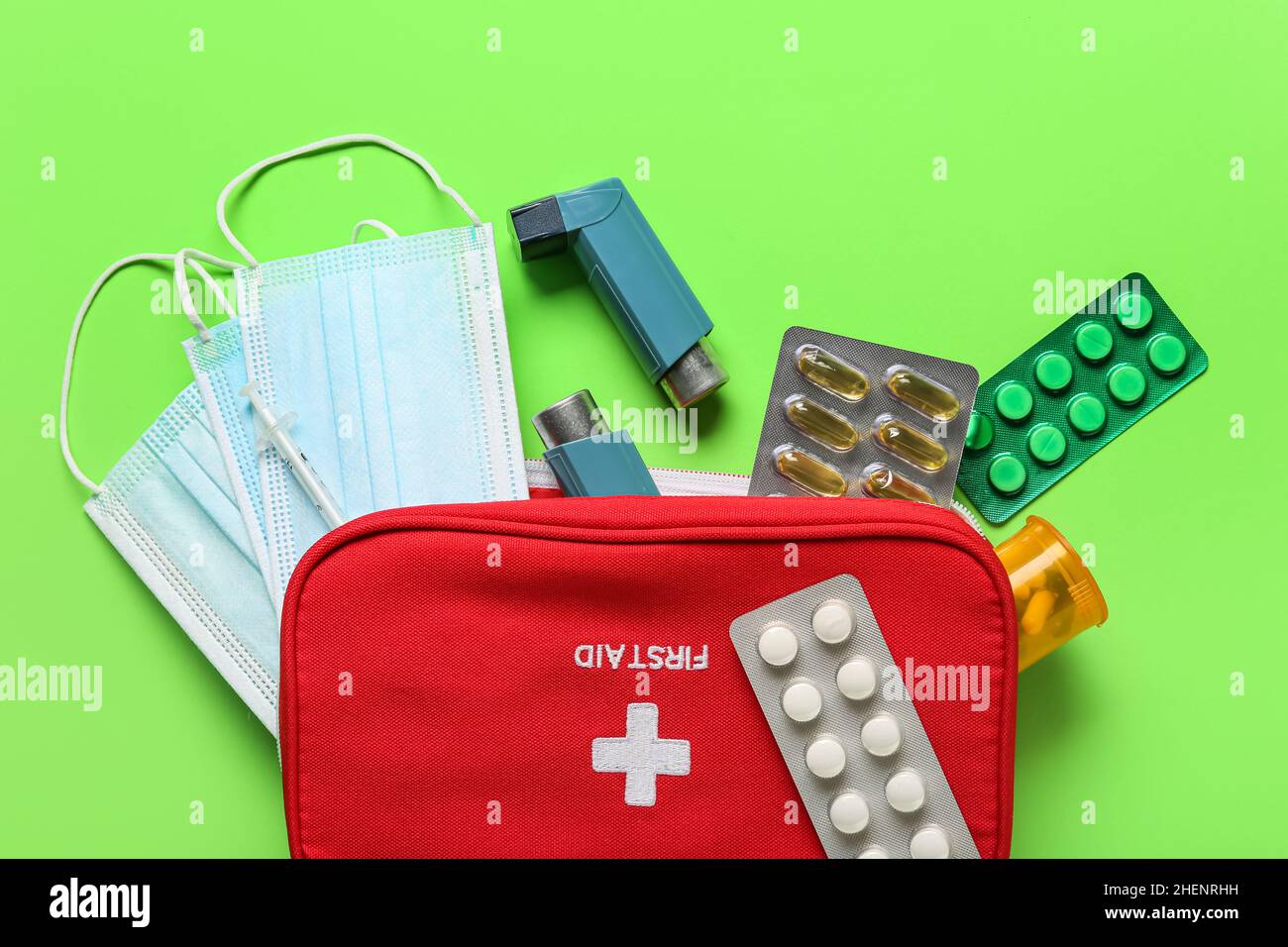 First aid kit with asthma inhalers, pills and masks on green background ...