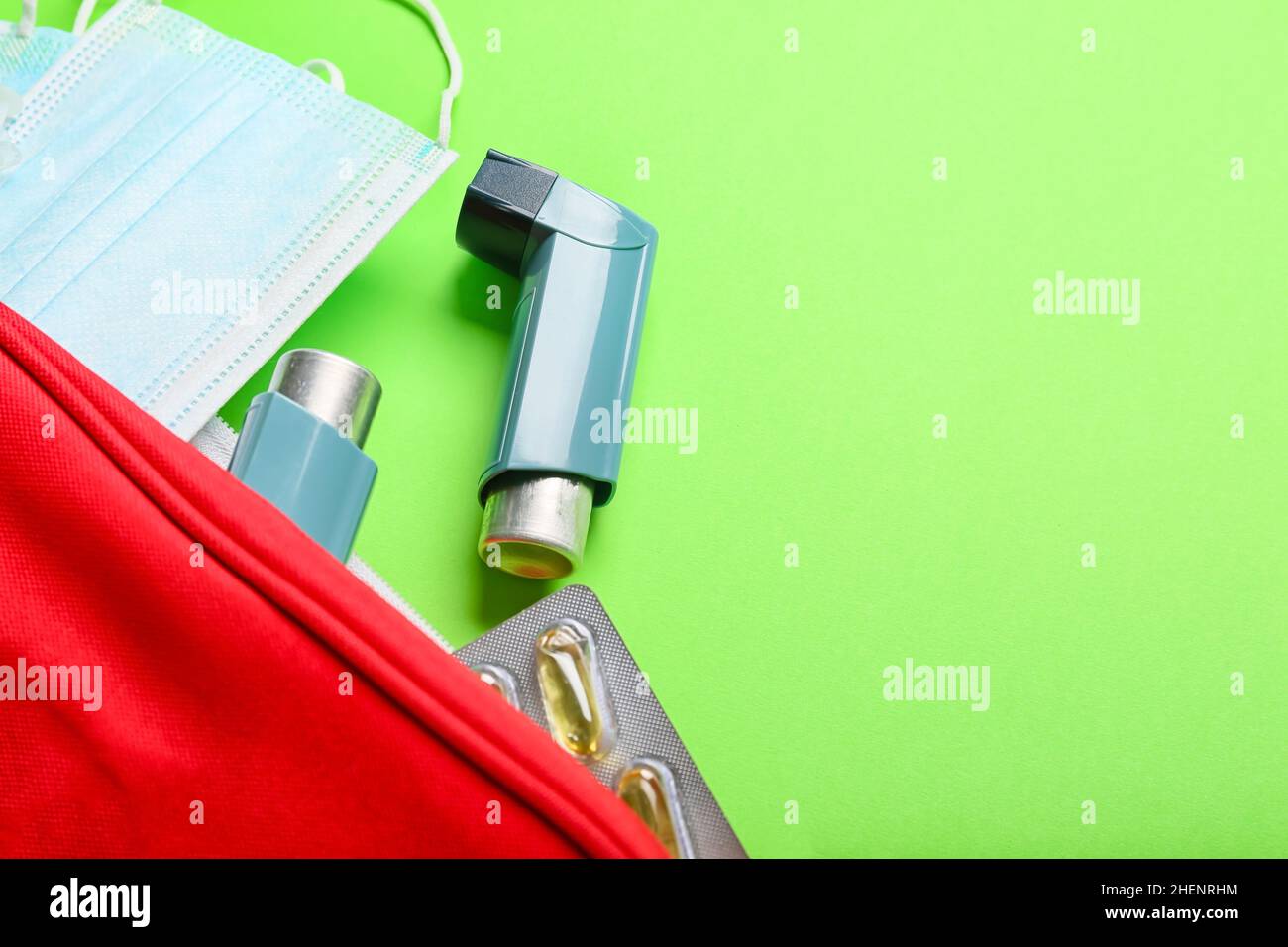 First aid kit with asthma inhalers, pills and mask on green background ...