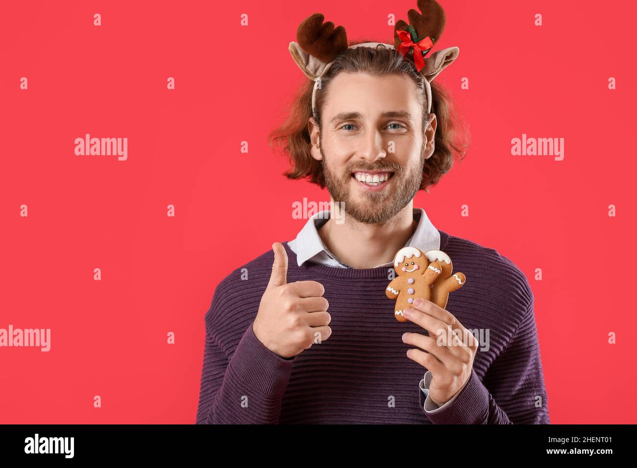 Handsome man in deer horns with gingerbread cookies showing thumb-up on ...