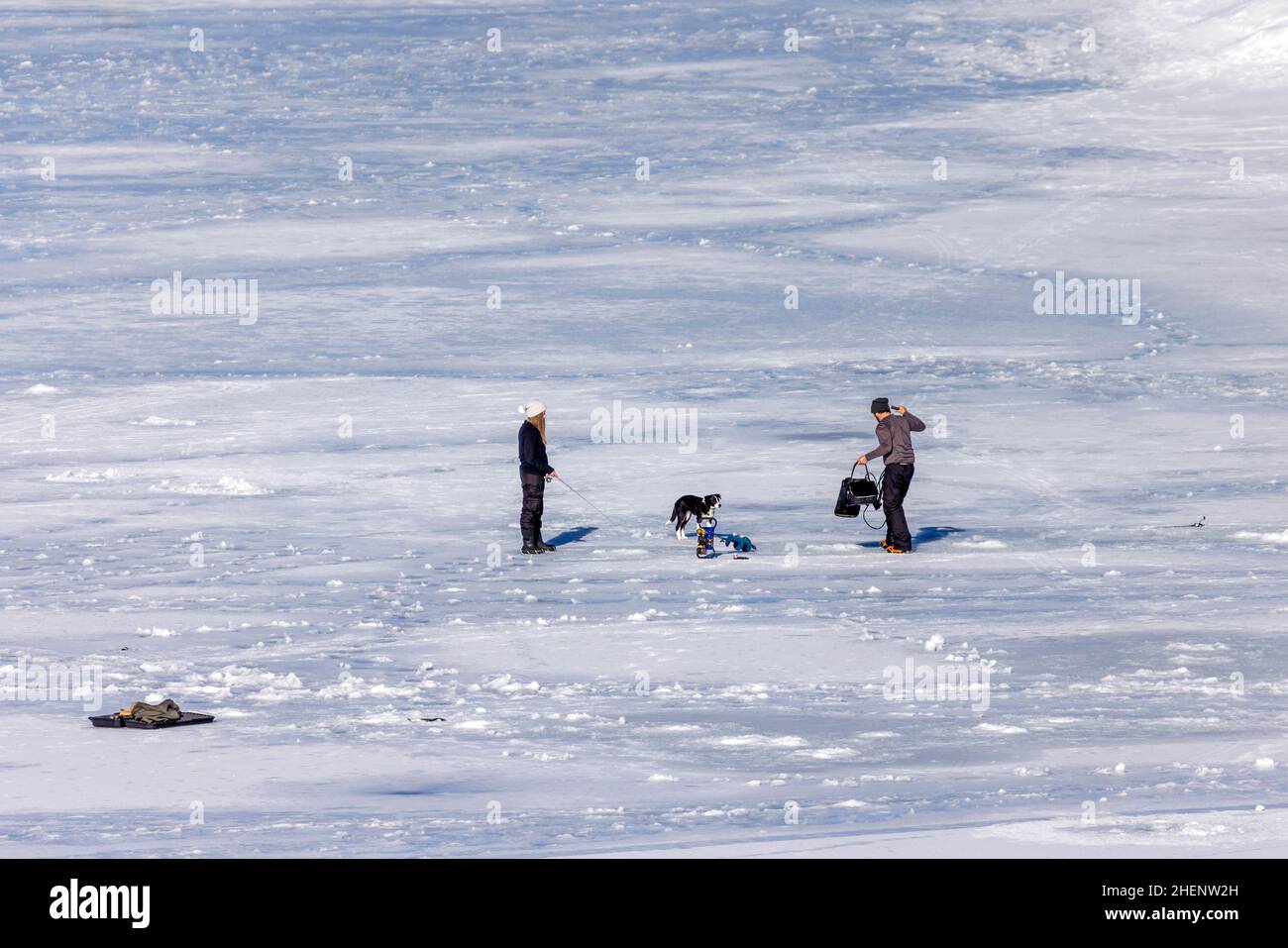 Couple and their dog set up on frozen lake surface for ice fishing ...