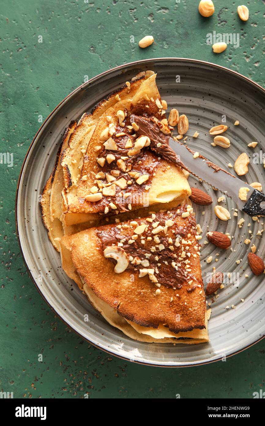 Plate of tasty thin pancakes with chocolate paste and nuts on green ...
