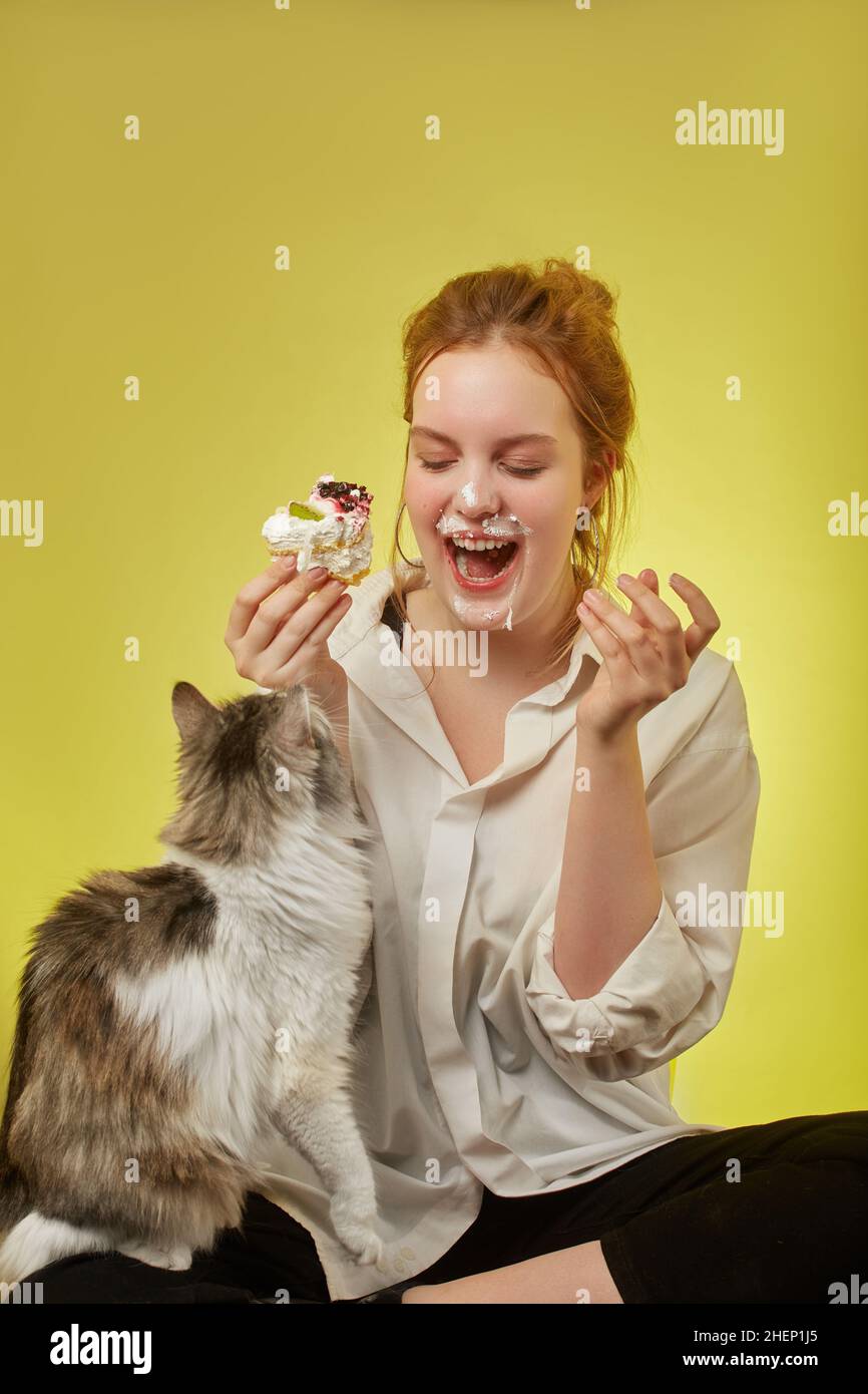 fun pretty red hair girl with cat eats sweet cherry dessert on yellow ...