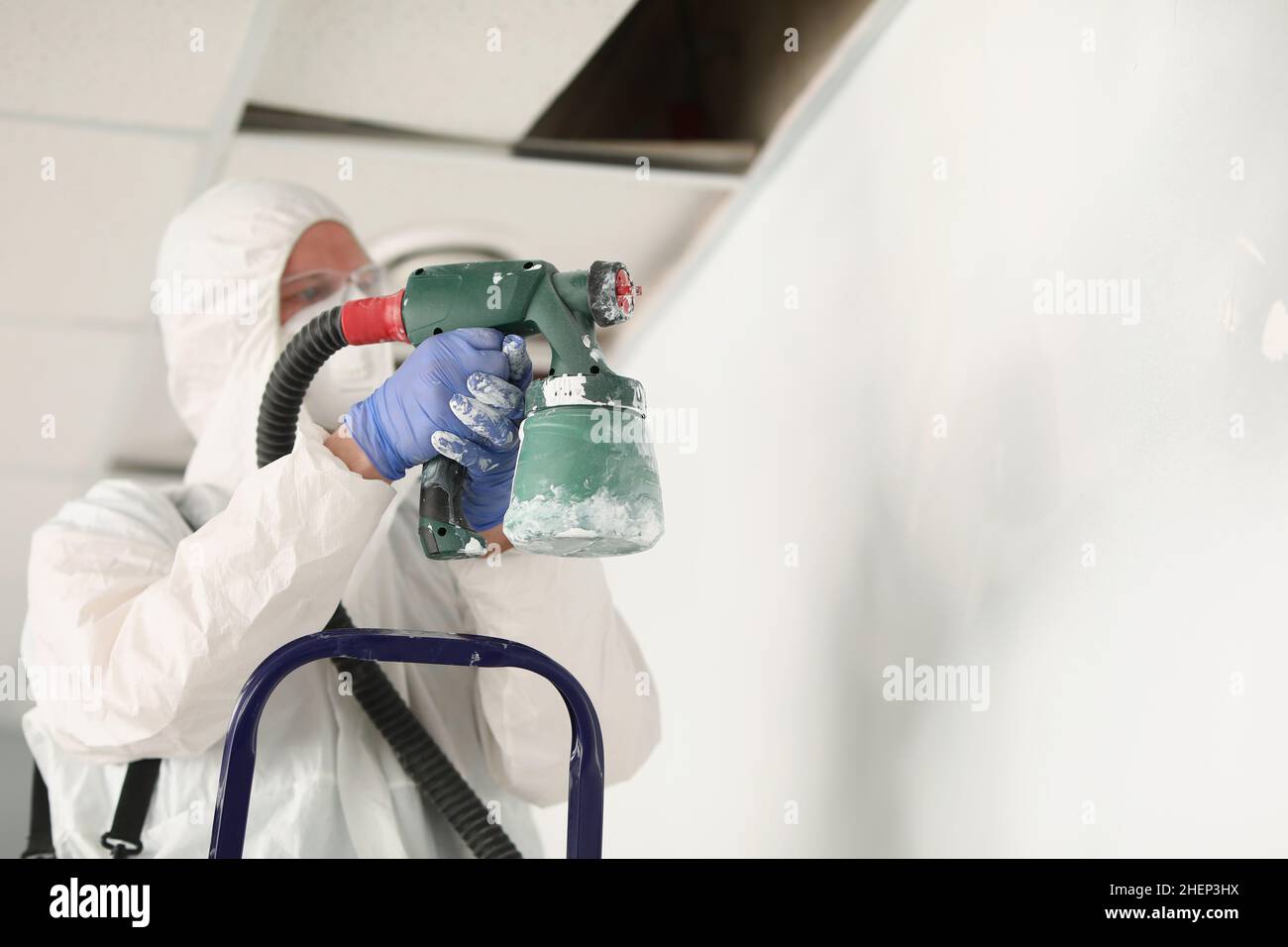 Male worker painting wall with spray gun in white colour, busy handyman ...