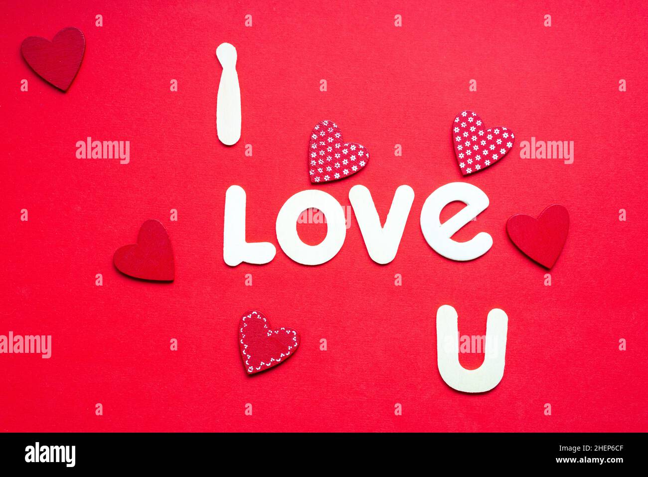 I love you writen with wooden letters on a red background with hearts ...