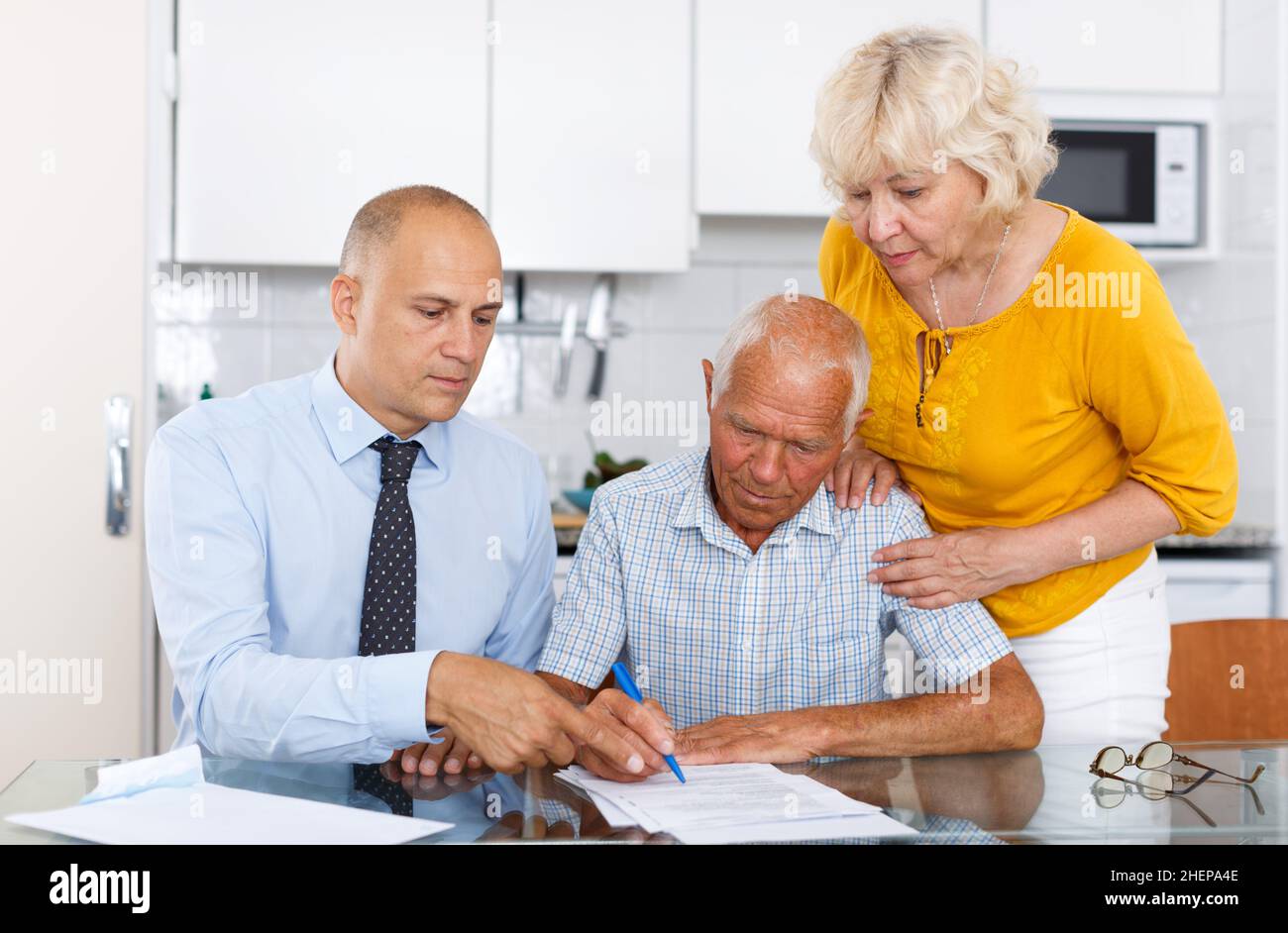Elderly husband and wife signing agreement papers with bank worker ...
