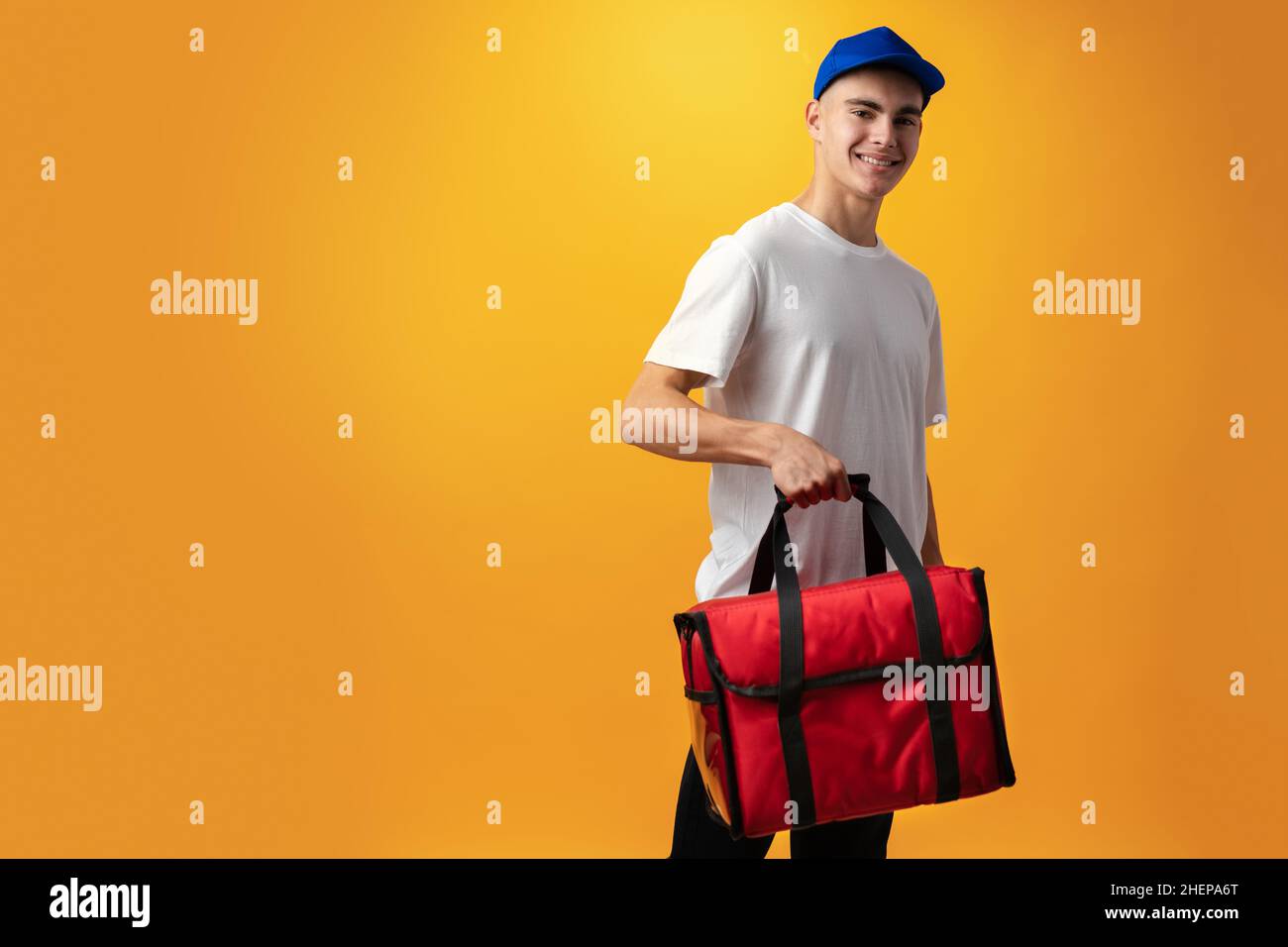 Portrait of pizza delivery boy with thermal bag against yellow ...