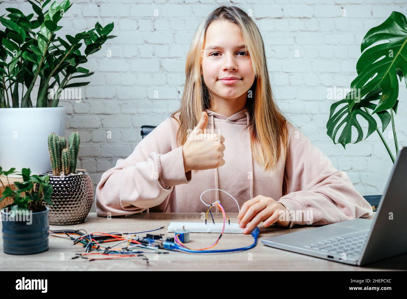 A teenager girl with her thumb up studying robotics at home, stem and arduino coding classes for ...