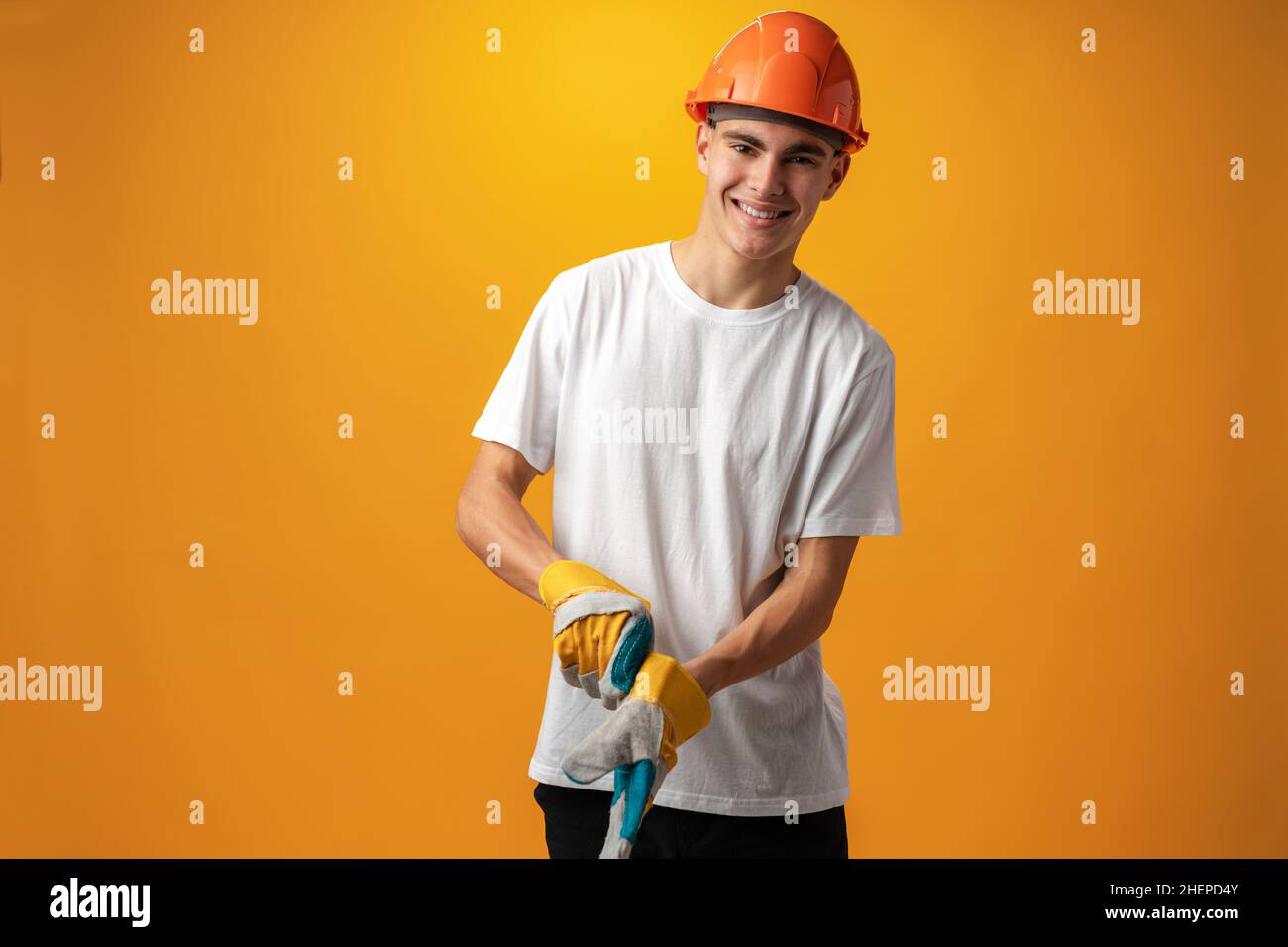 Confident smiling teen boy wearing orange hard hat against yellow ...
