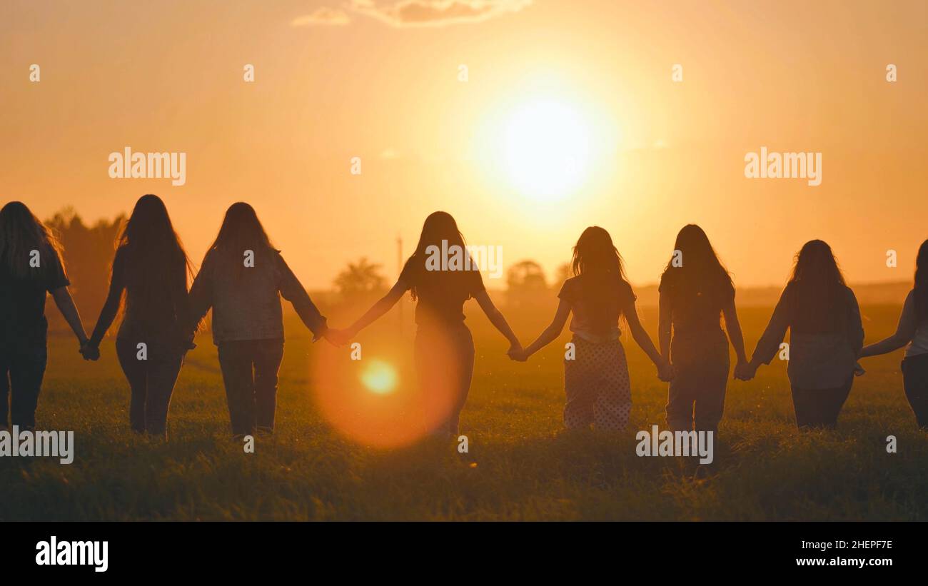 A group of girls walk towards the sun at sunset holding hands Stock ...