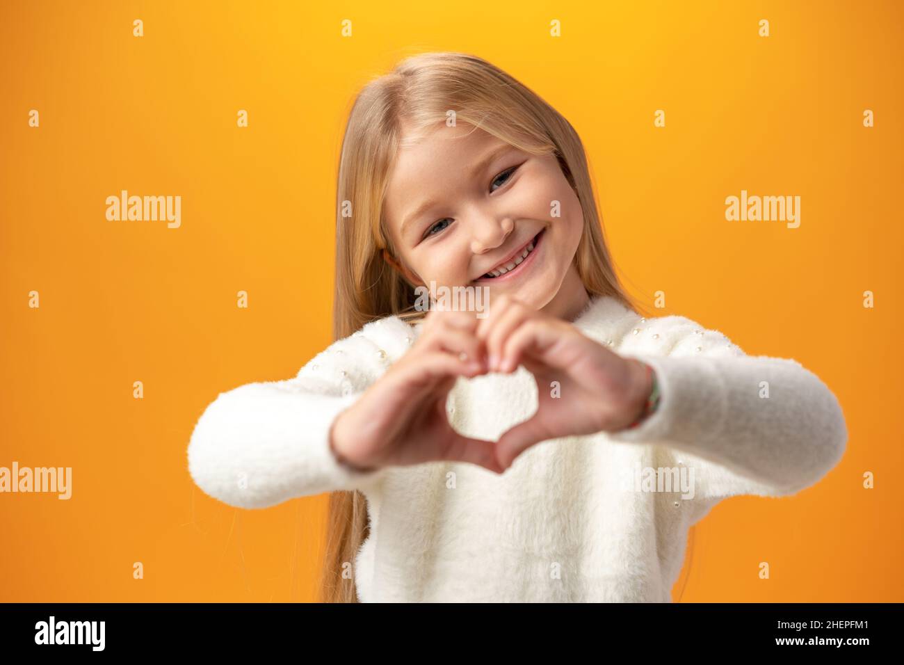 Happy little girl showing heart love gesture over yellow background ...