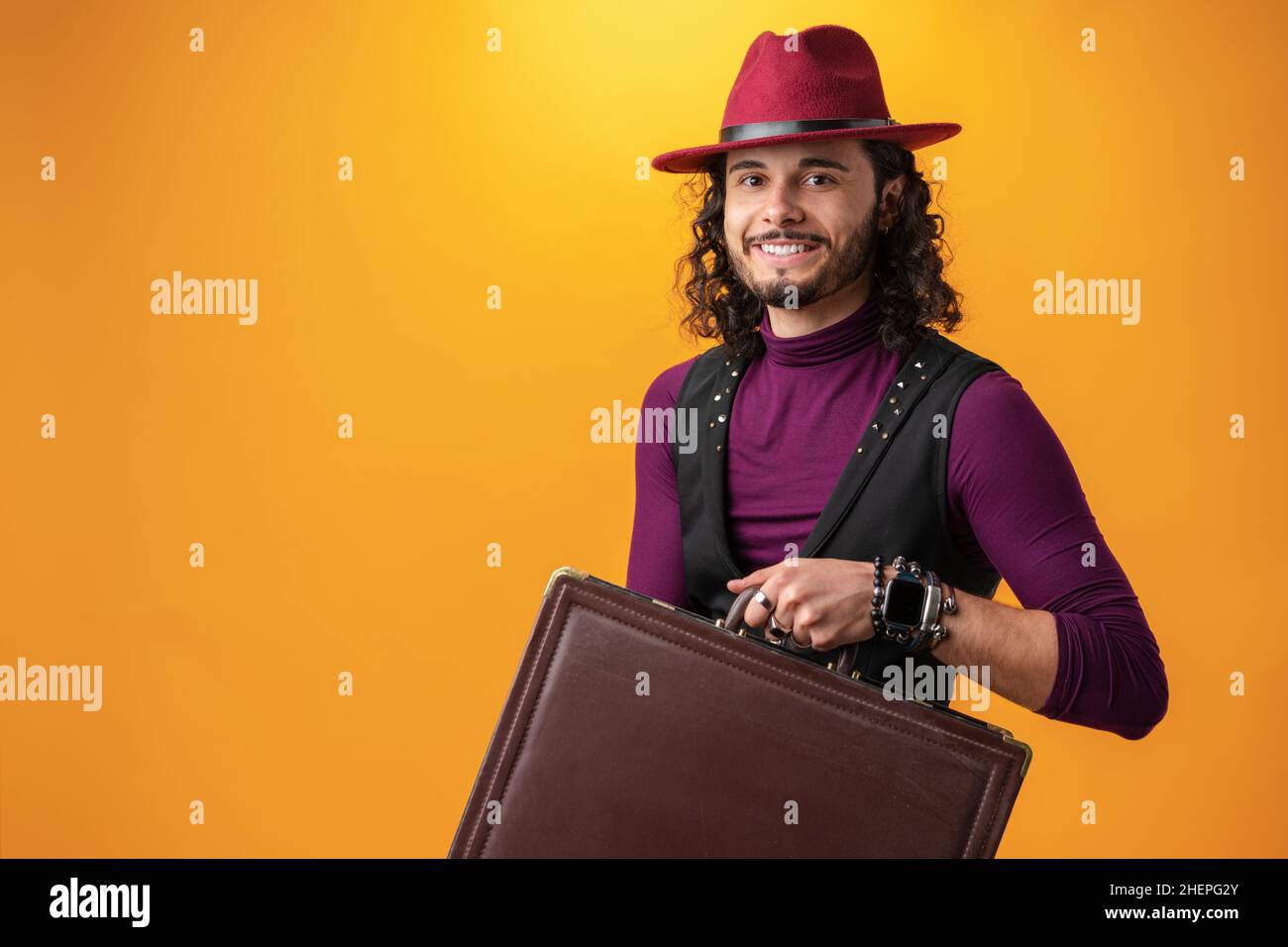 Young man with cirly long hair showing a briefcase against yellow ...