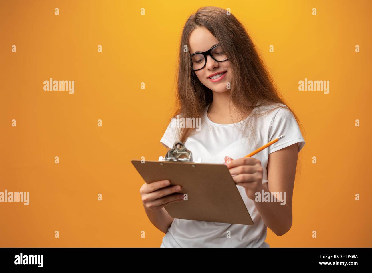Teen school girl taking notes on clipboard against yellow background ...