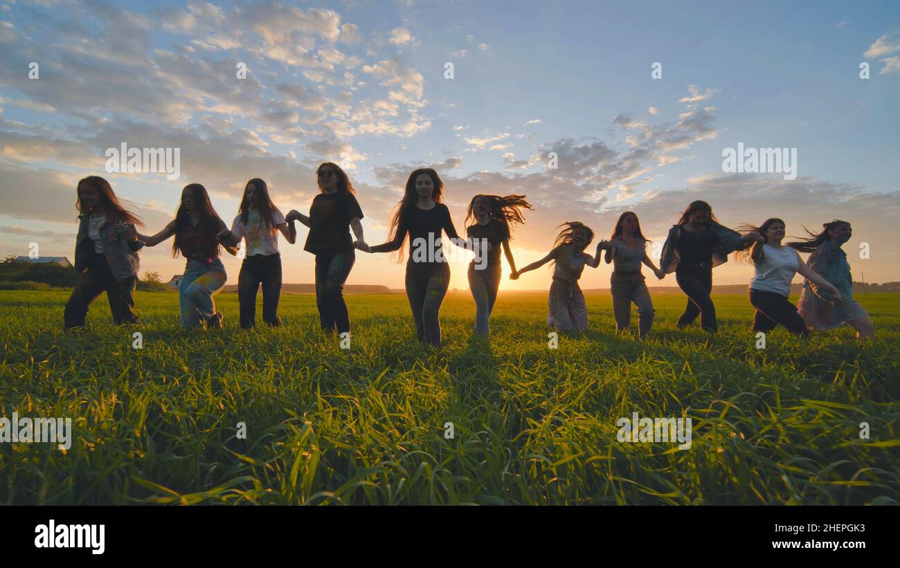 A group of girls walk towards the sun at sunset holding hands Stock ...
