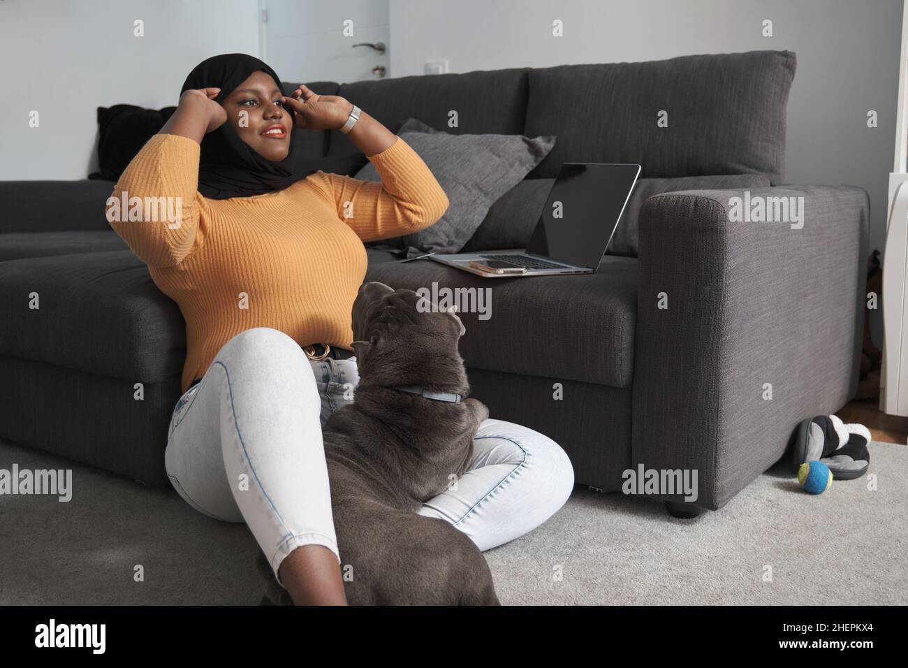 Young muslim woman fixing the hijab sitting with her grey sharpei dog ...