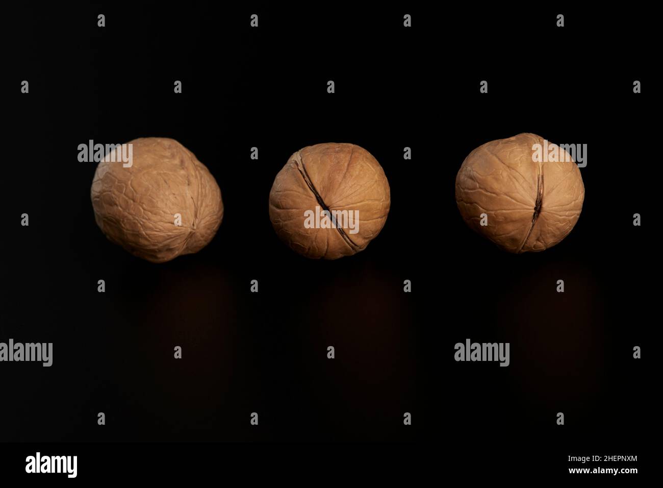 Three inshell walnuts lie in a row on a black background Stock Photo ...