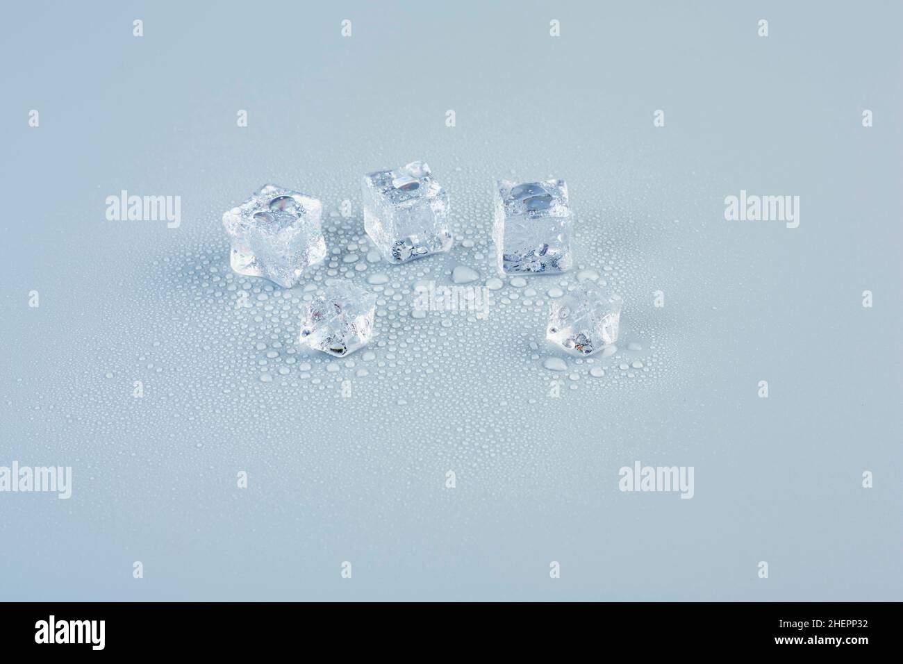 Ice cubes scattered on a table on a gray background in drops of melt ...