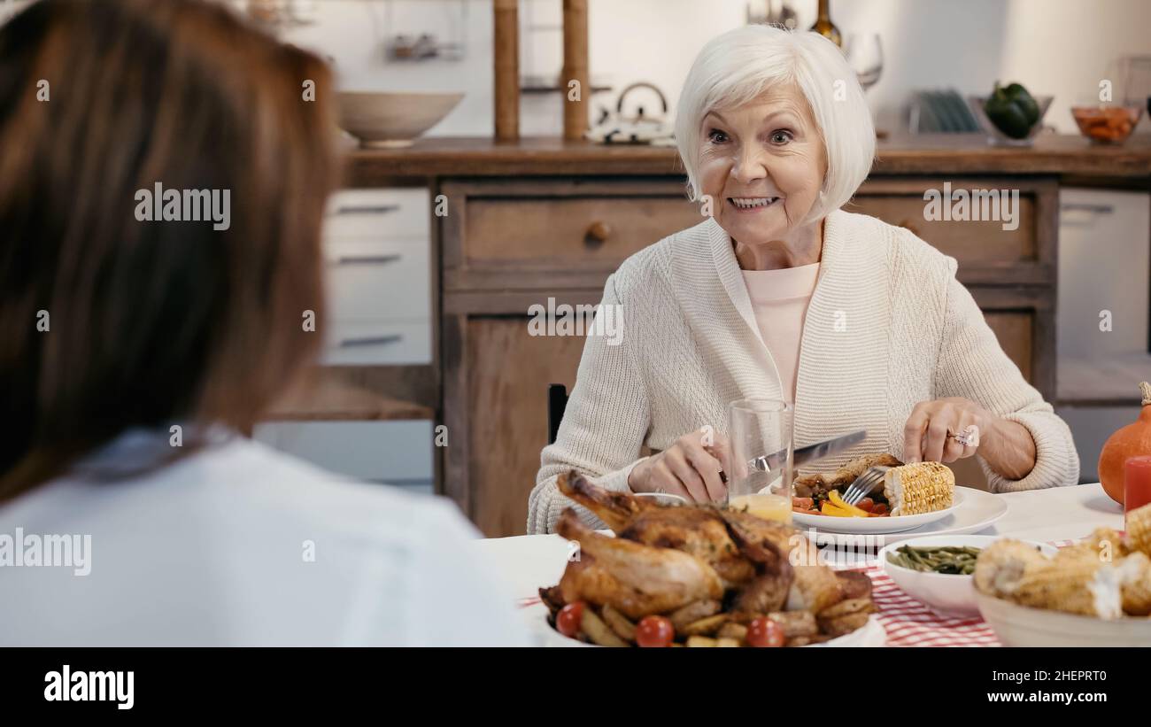 senior woman smiling during thanksgiving dinner with blurred guest ...