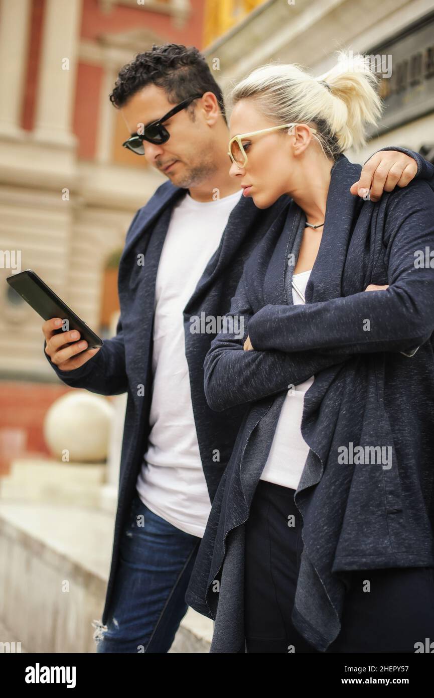 Beautiful couple sitting on steps of monument and looking at tablet ...