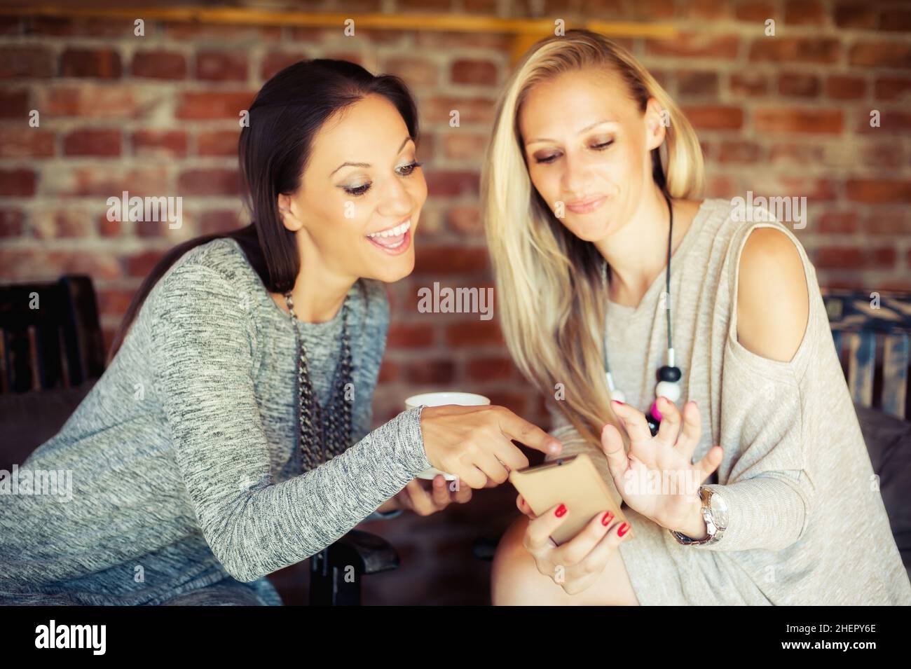 Two happy young female friends with coffee cups enjoying a conversation ...