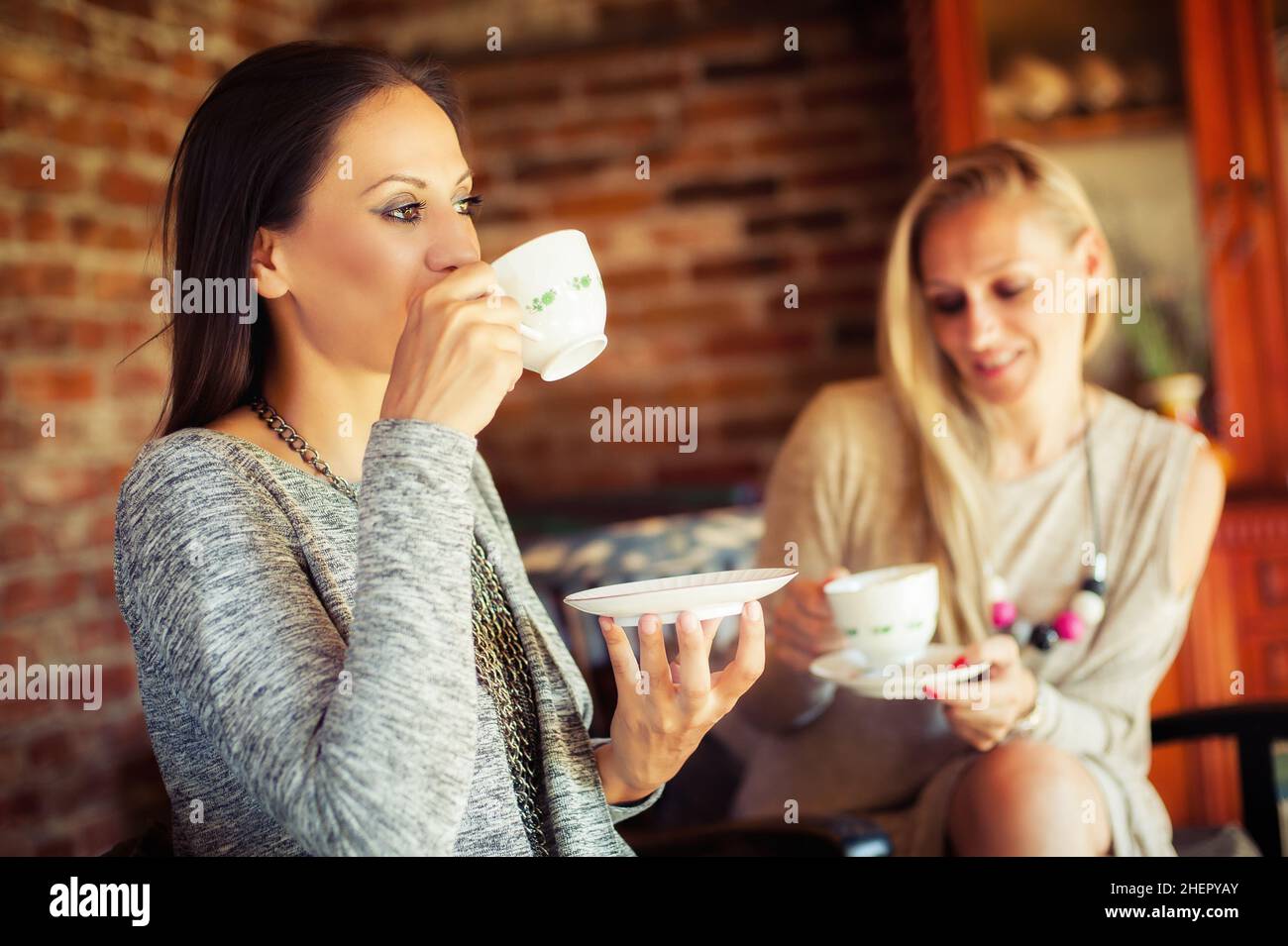 Two happy young female friends with coffee cups enjoying a conversation ...