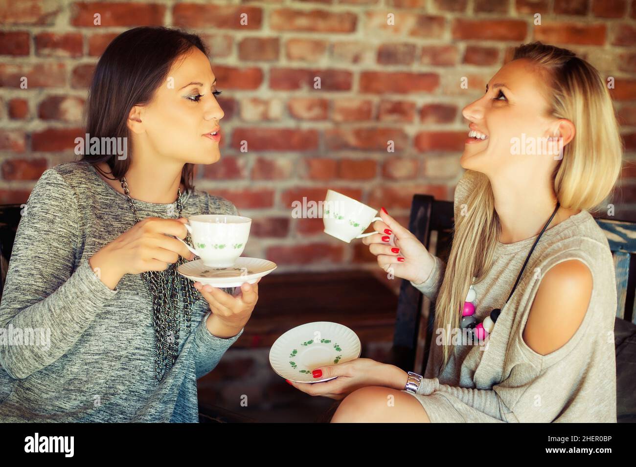 Two happy young female friends with coffee cups enjoying a conversation ...