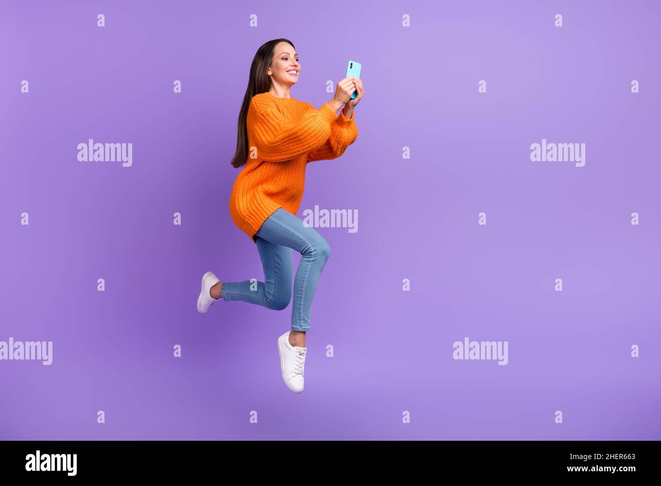 Photo of energetic active lady hold phone read chat jump wear orange ...