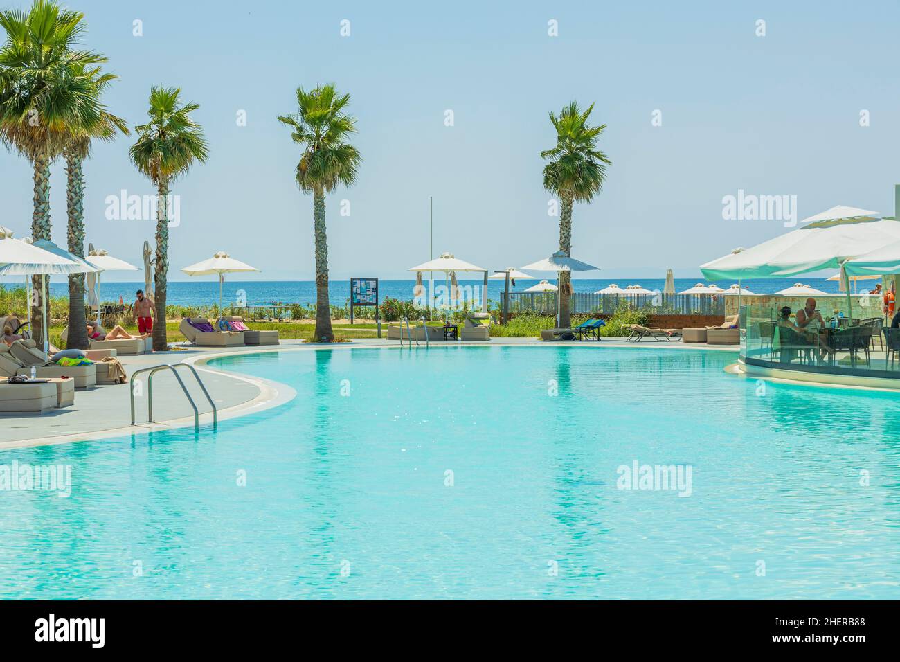 View of outdoor pool and people on sun beds and in pool bar on sunny ...