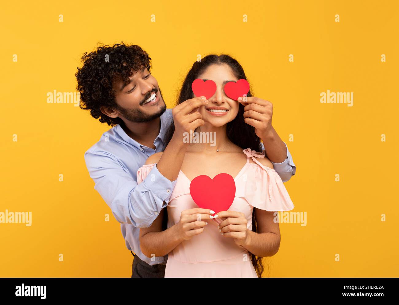 Affection. Loving indian husband covering wife's eyes with paper hearts ...