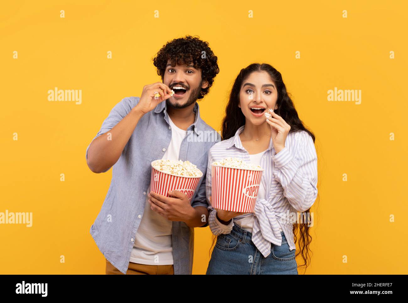 Excited indian man and woman eating popcorn at cinema, standing over ...