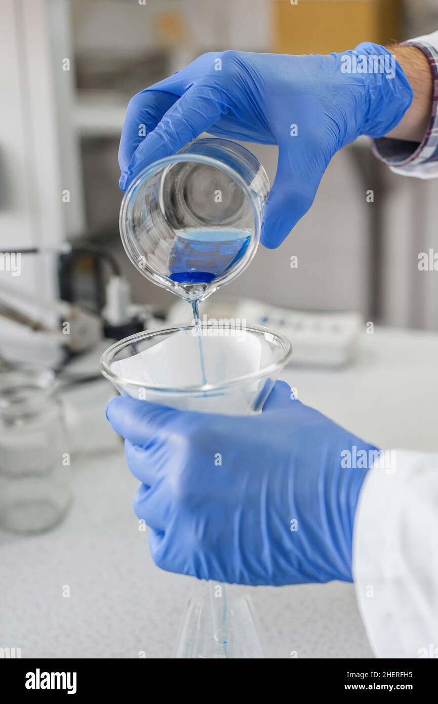 Scientific laboratory technician performs tests and pouring blue liquid ...