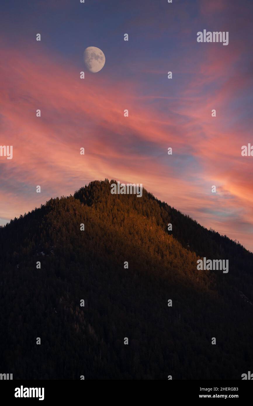 forested mountain peak with moon at sunset and burning clouds Stock ...
