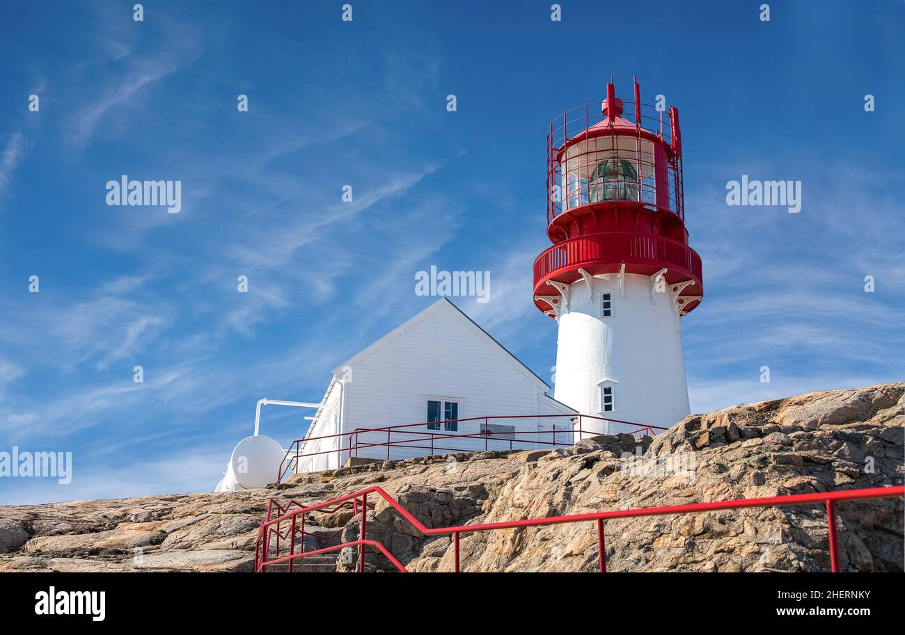 A red lighthouse near a white house on the rocks in the blue ocean ...