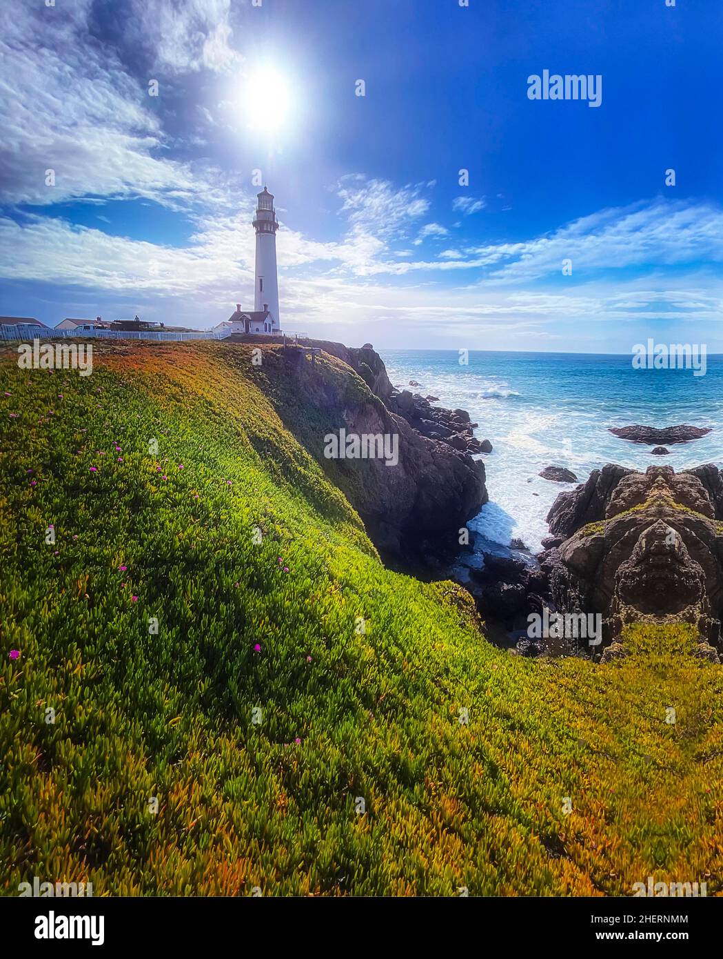 Lighthouse near the ocean surrounded by rocks with clouds and blue sky ...