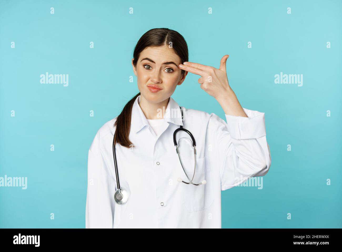 Tired and annoyed young woman showing pictol shot gesture over head ...