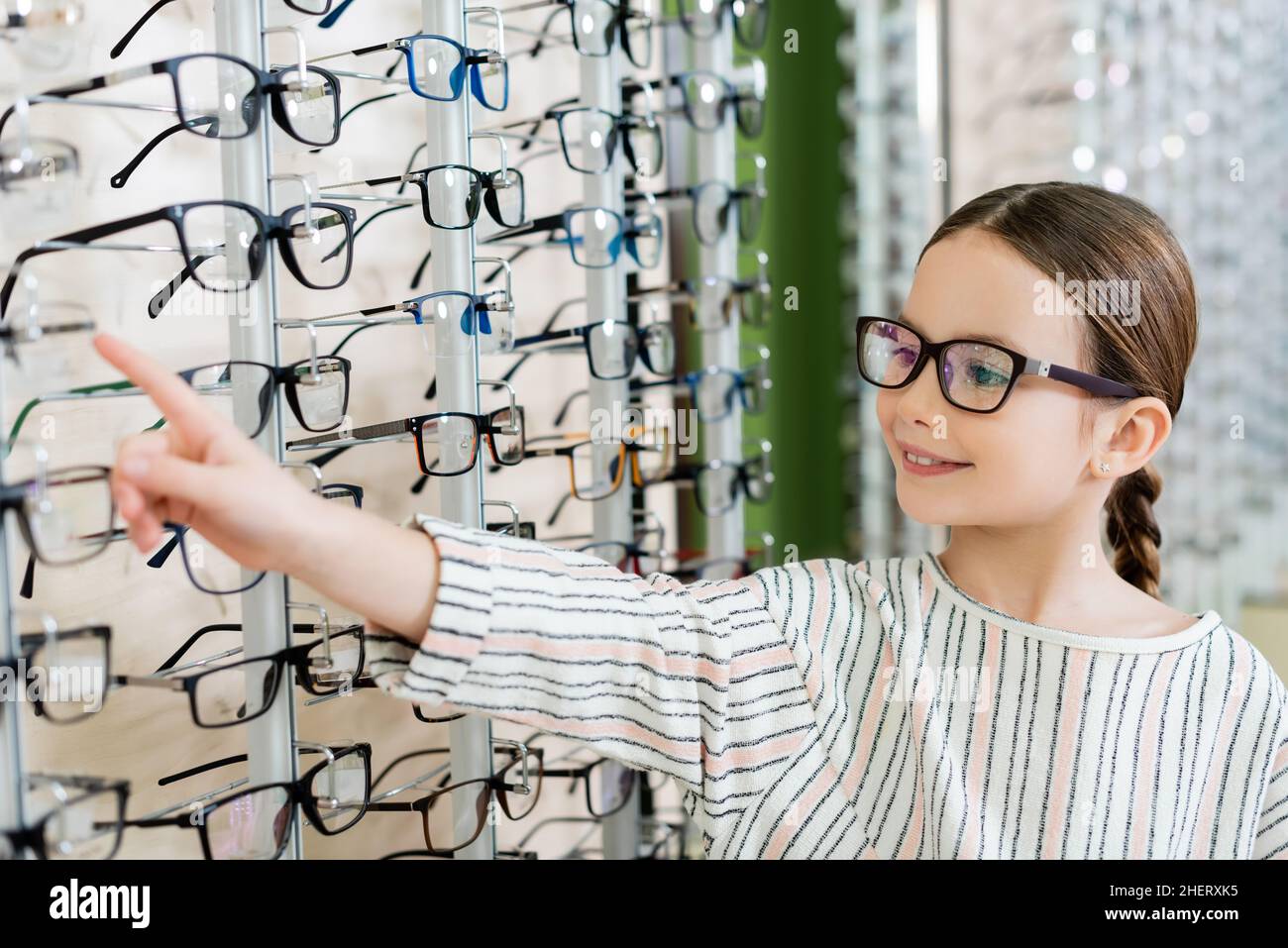positive child pointing at assortment of eyeglasses in optics shop ...