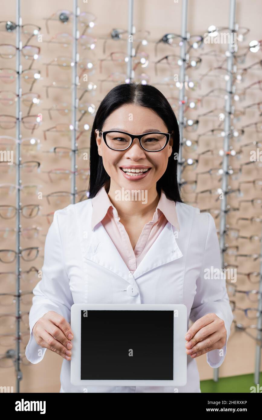 happy asian oculist in eyeglasses holding digital tablet with blank ...
