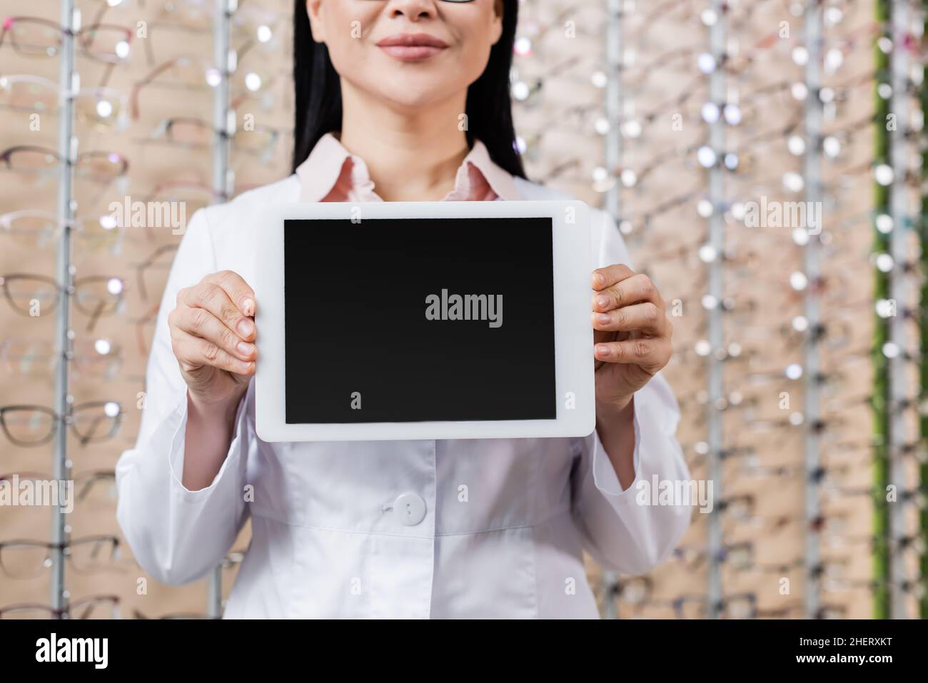 cropped view of blurred oculist in white coat holding laptop with blank ...