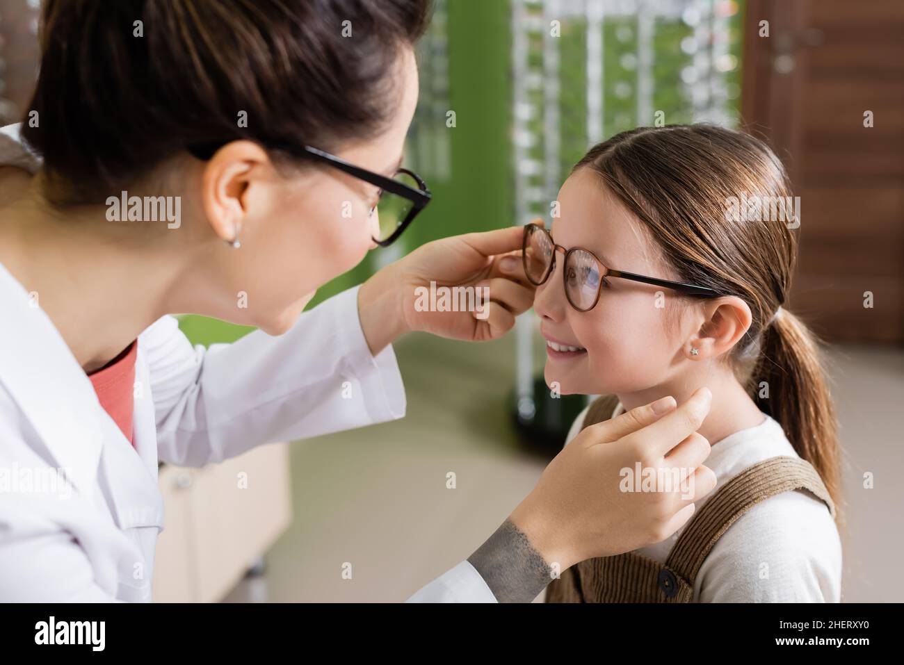 oculist putting eyeglasses on cheerful girl in optics salon Stock Photo ...