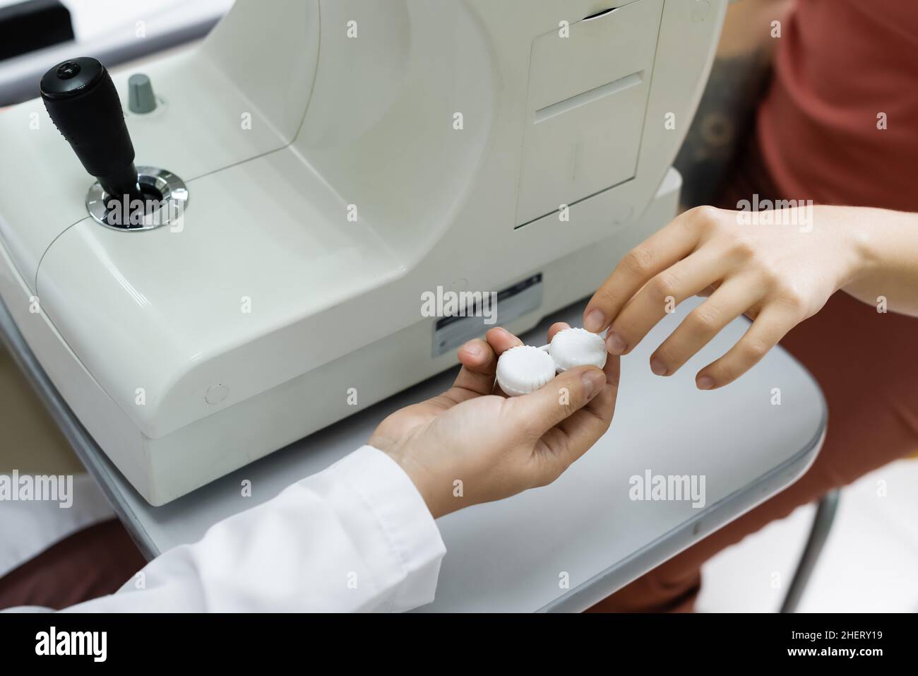 partial view of optometrist giving lens case to patient near ...