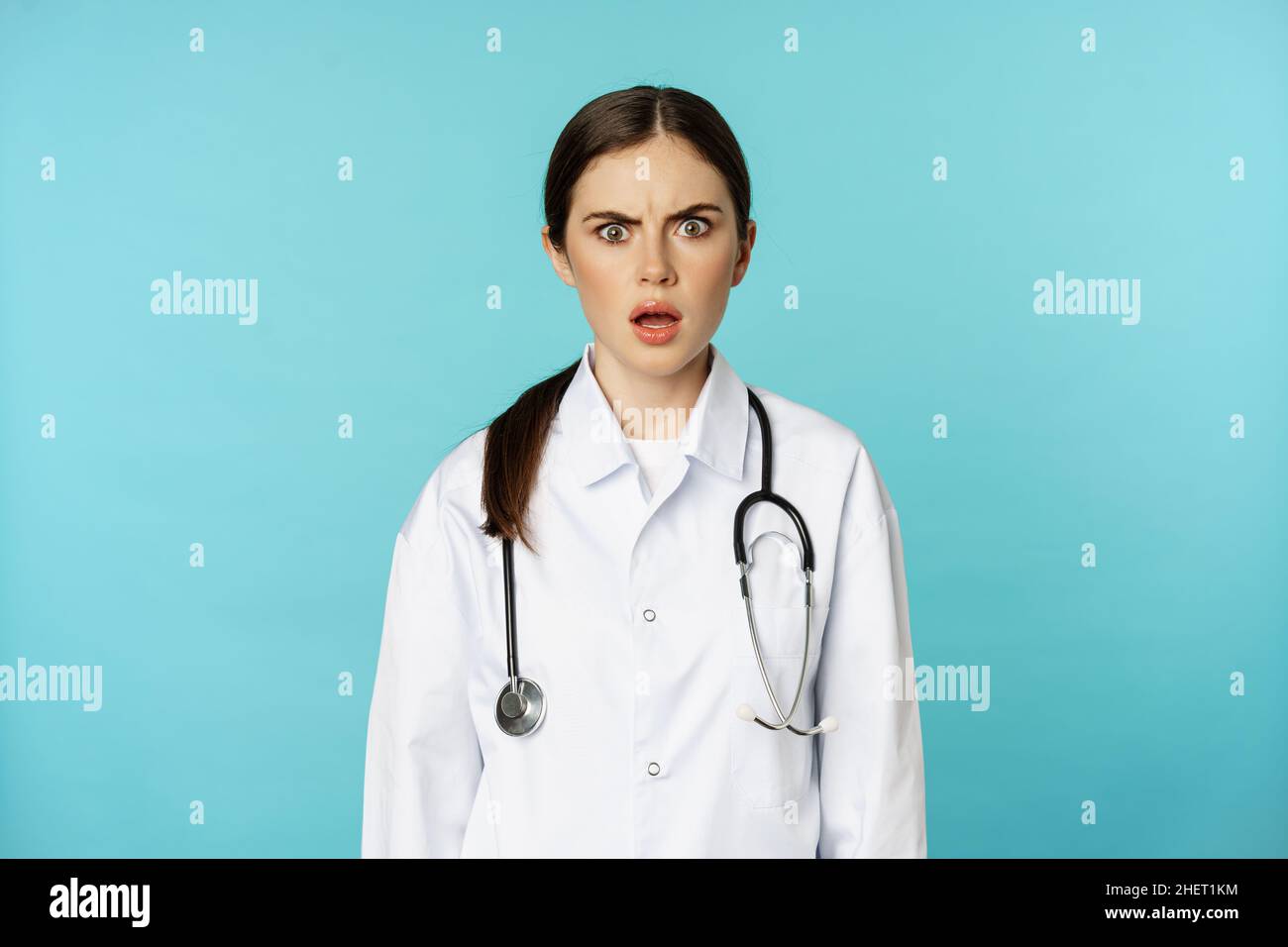 Portrait of shocked woman doctor, female hospital intern in white coat ...